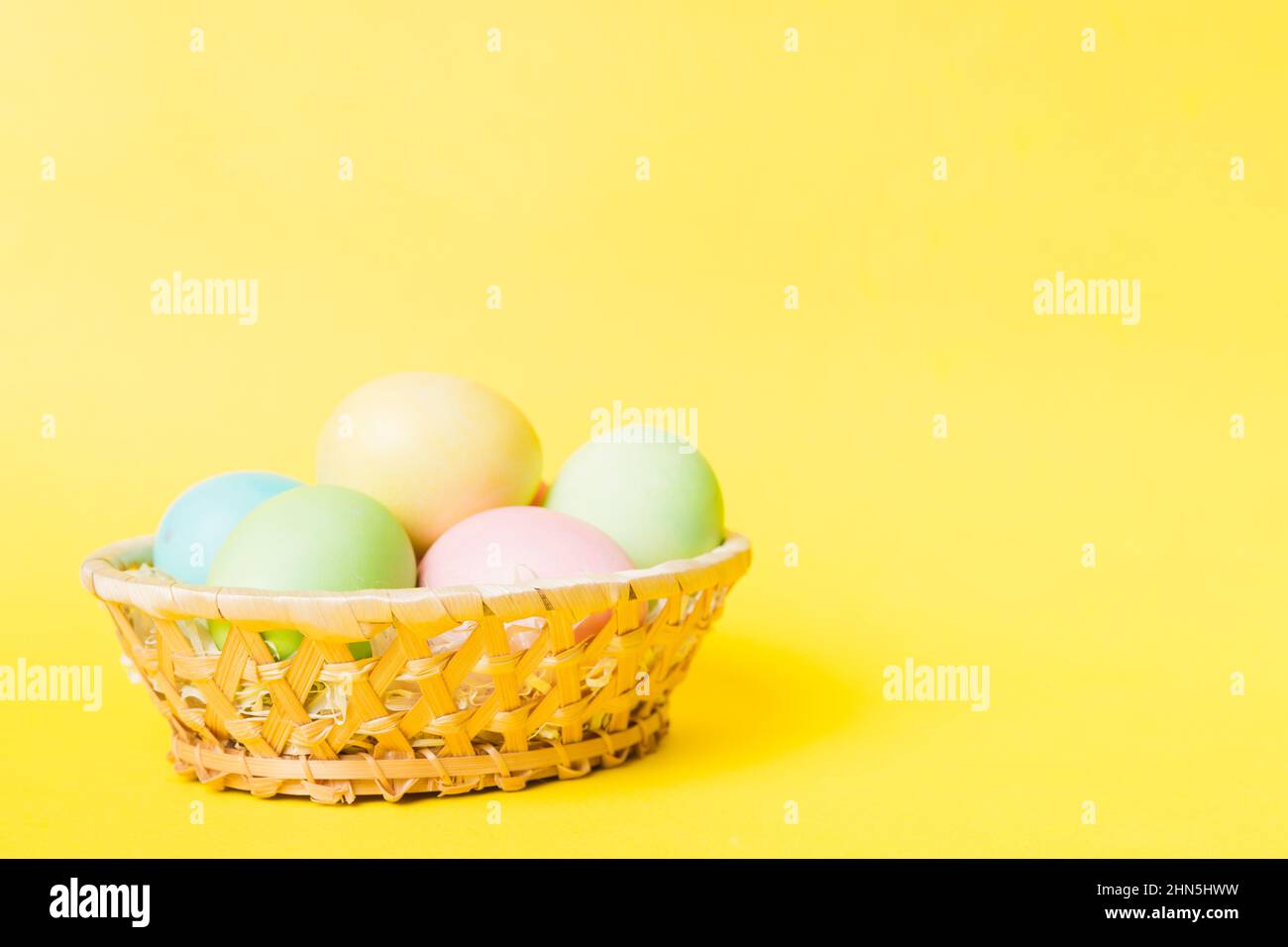 Multi colors Easter eggs in the woven basket on colored background ...