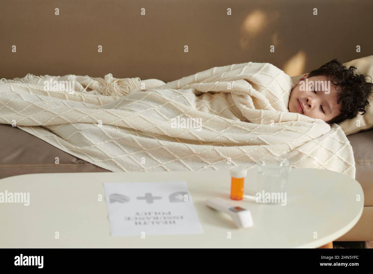 Sick boy with fever sleeping on sofa in living room after taking ...