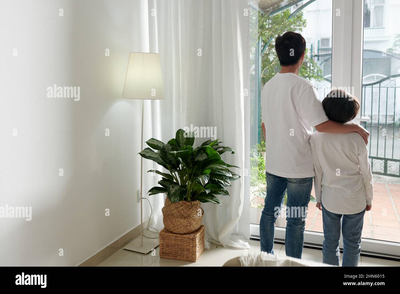 Father hugging his preteen son when they are looking at house gate ...