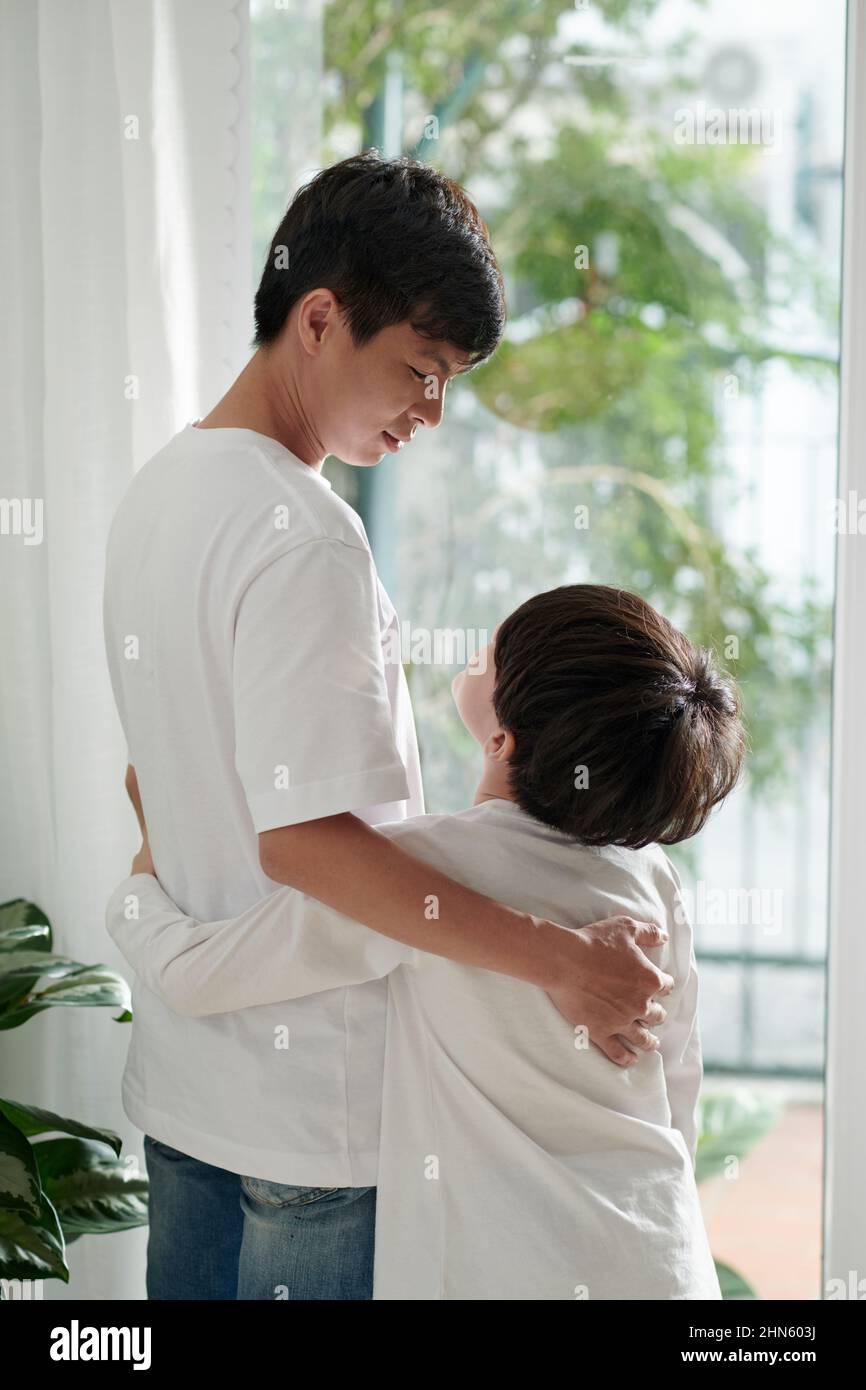 Boy hugging his father and asking him question, view from the back ...