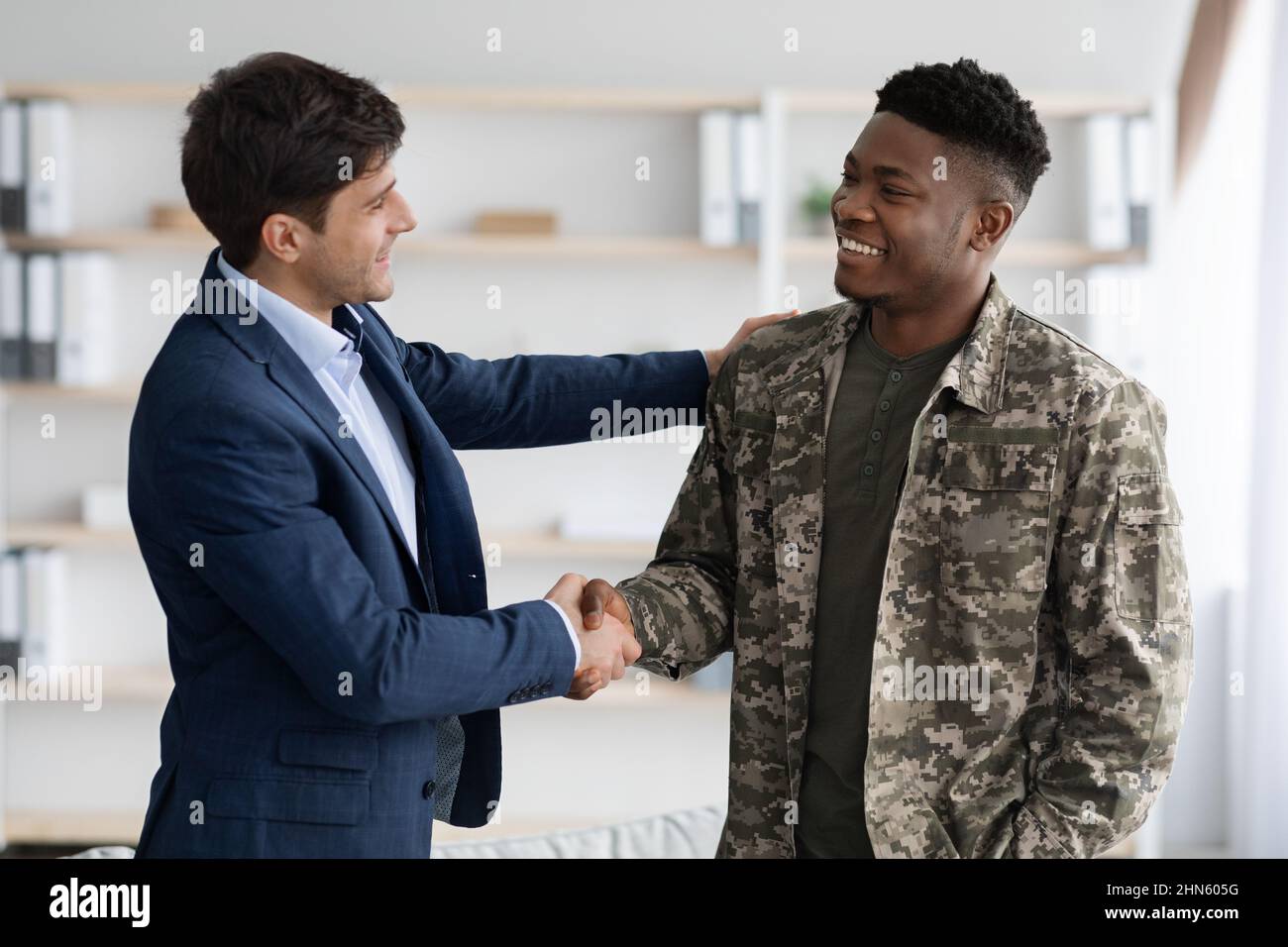 Cheerful guy in suit shaking black military man hand Stock Photo - Alamy