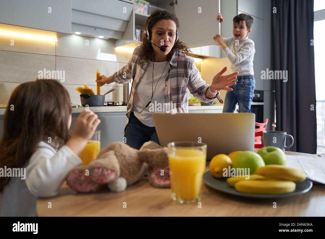 Woman having business call while cooking and calming children down ...