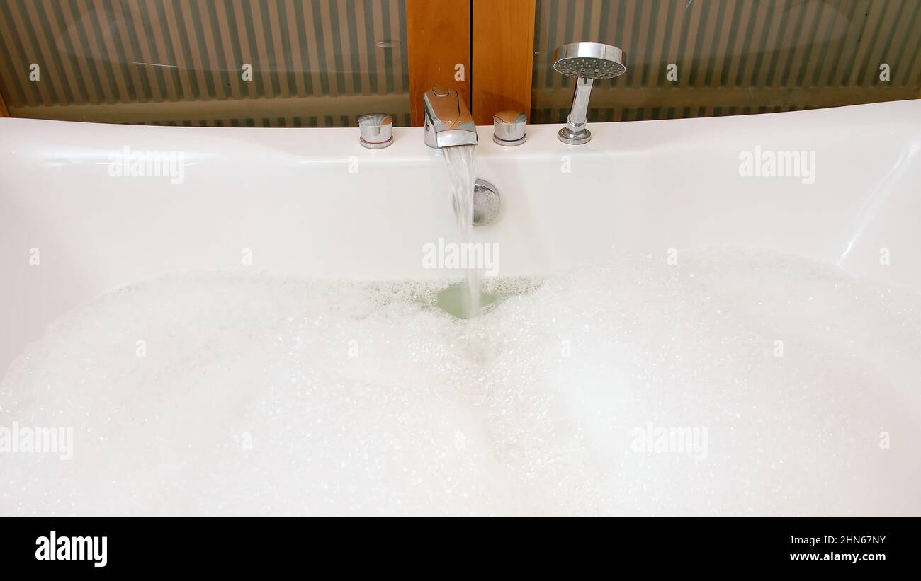 Bathtub with soap suds. Preparing a bath, hot water flows from the tap ...