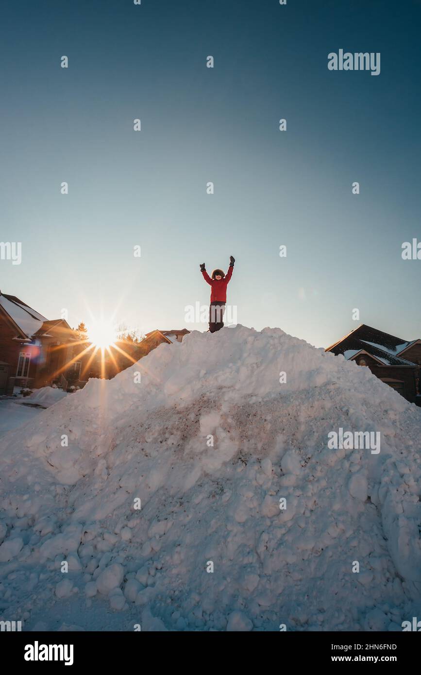 Child in winter jacket climbing big snow pile on a residential street ...