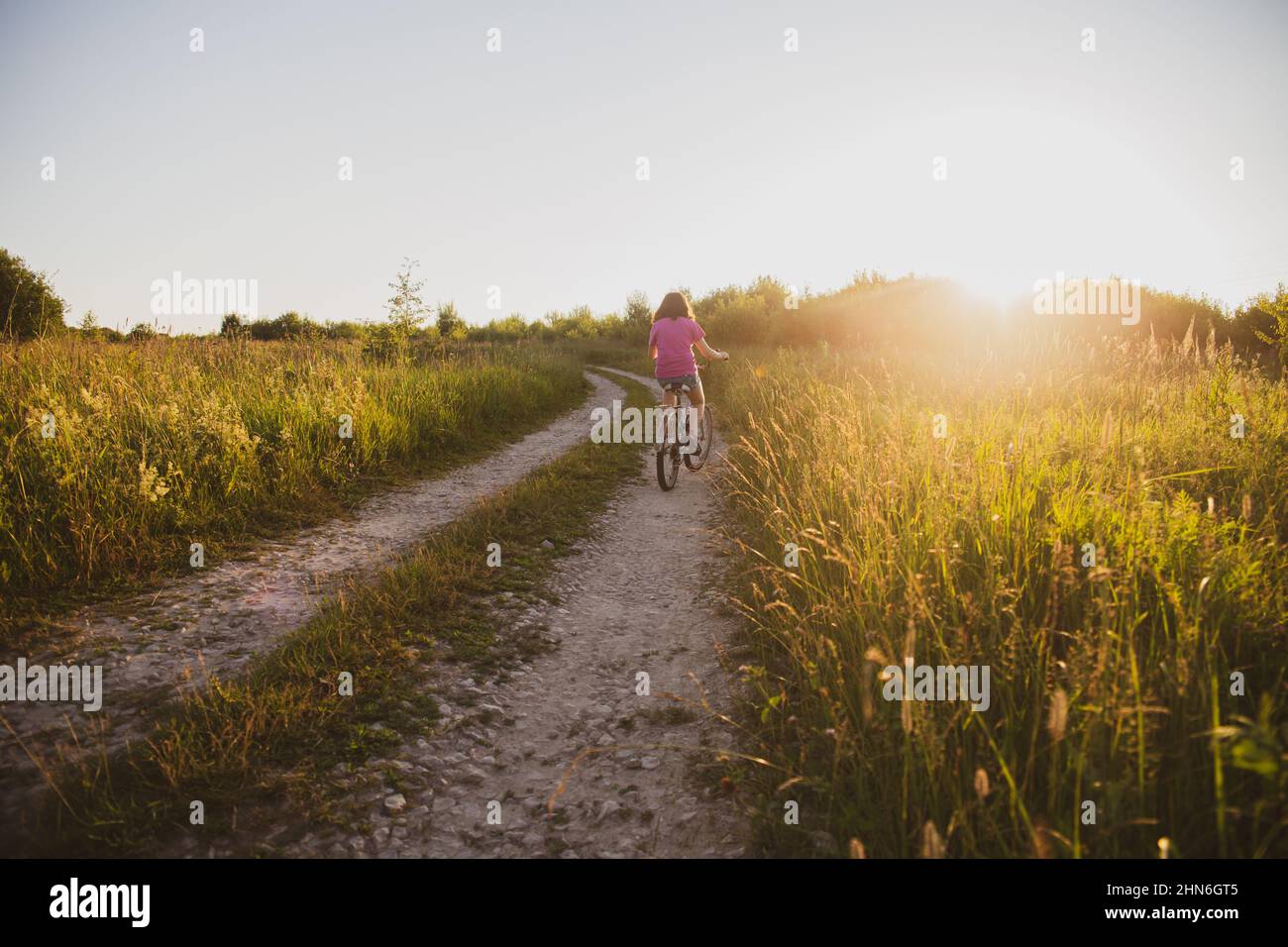 A teenage girl rides a bicycle along a country road in a field Stock ...