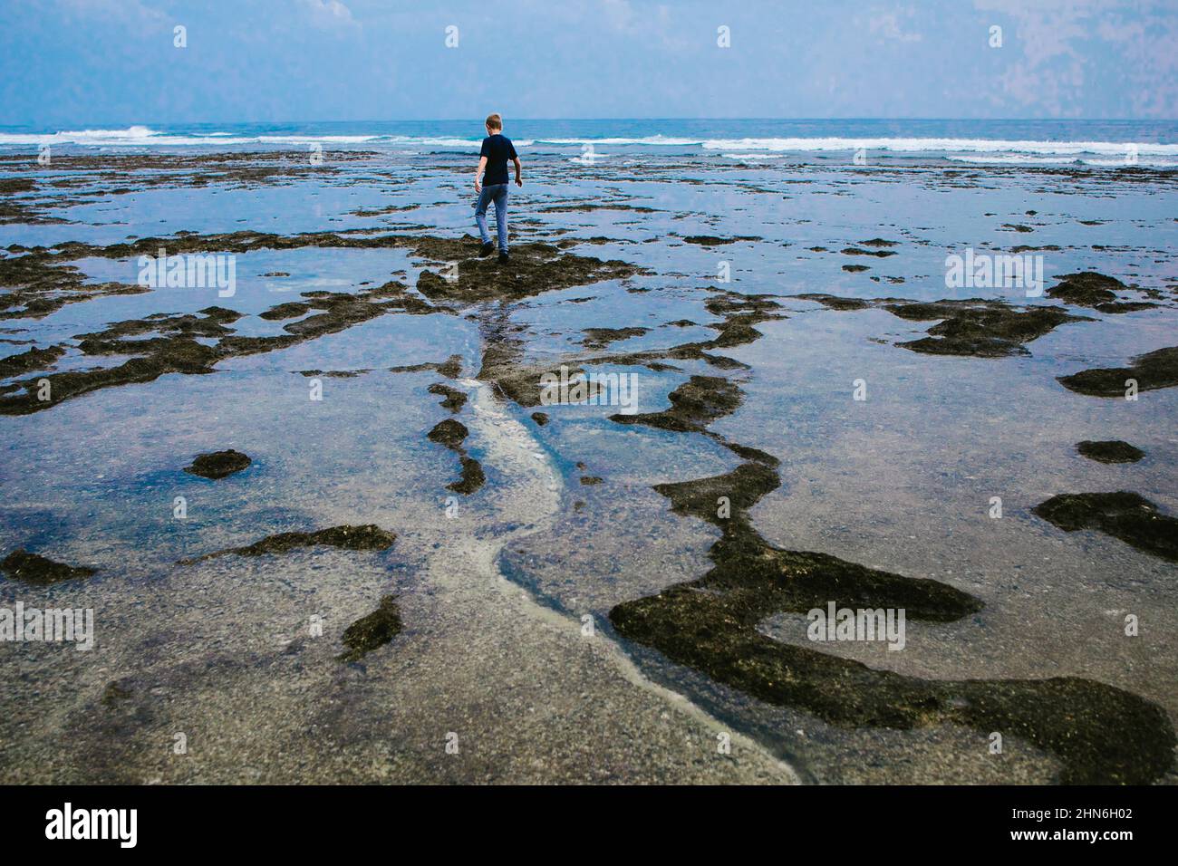Boy walking out to sea on a path of sand through tide pools Stock Photo ...