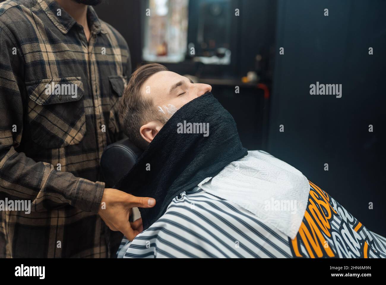 Barber preparing man face for shaving with hot towel in barber shop ...