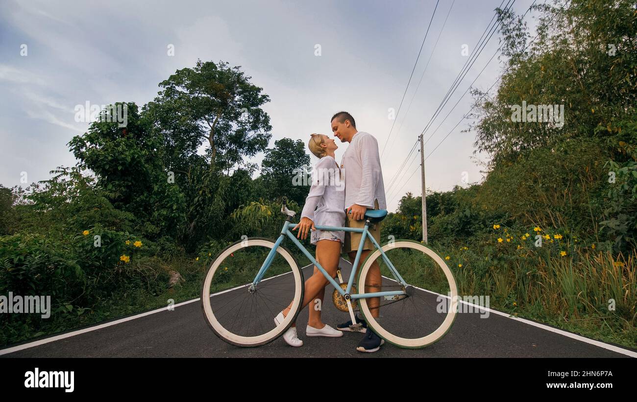 Biking road trip. Love couple on blue bike in white clothes on forest road. Just married woman ...