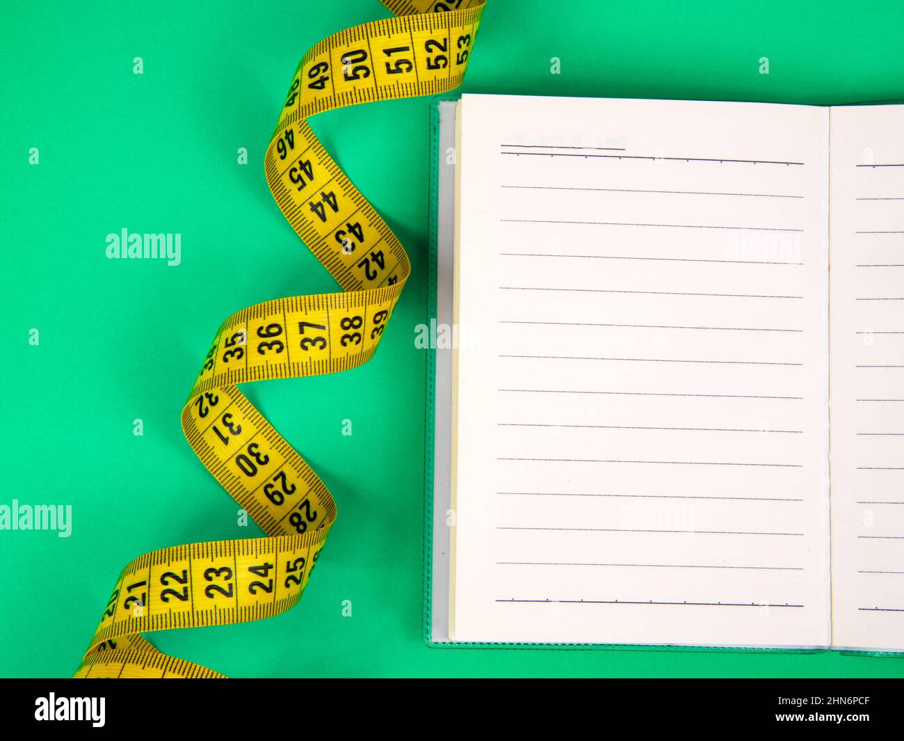 Yellow tape measure centimetric with paper note on green background ...