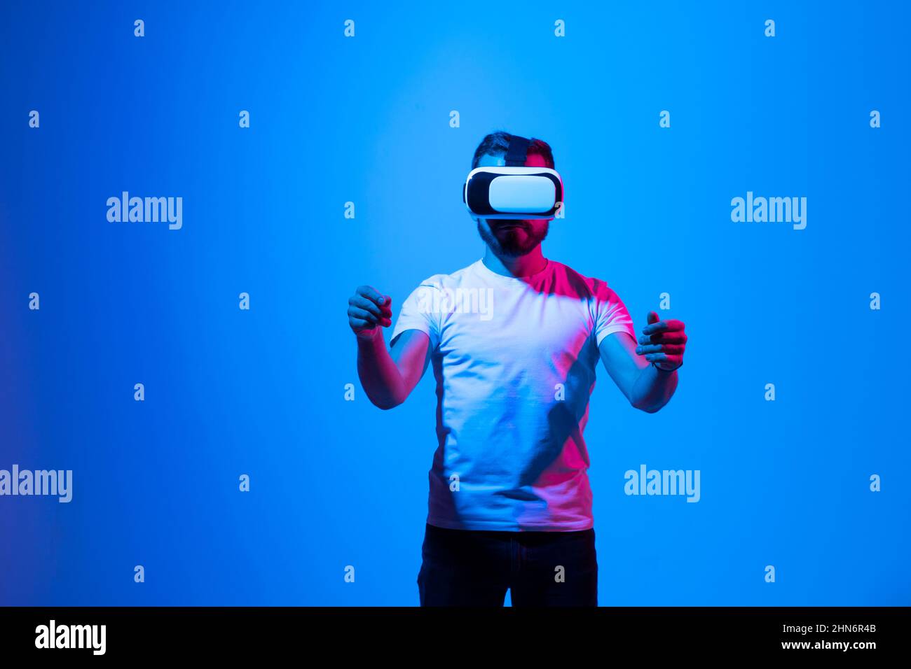 Man use a VR headset and stands as he hold something in virtual space ...