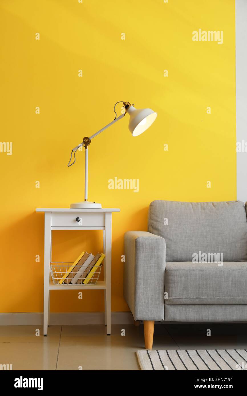 Table with glowing lamp and grey sofa near color wall Stock Photo - Alamy