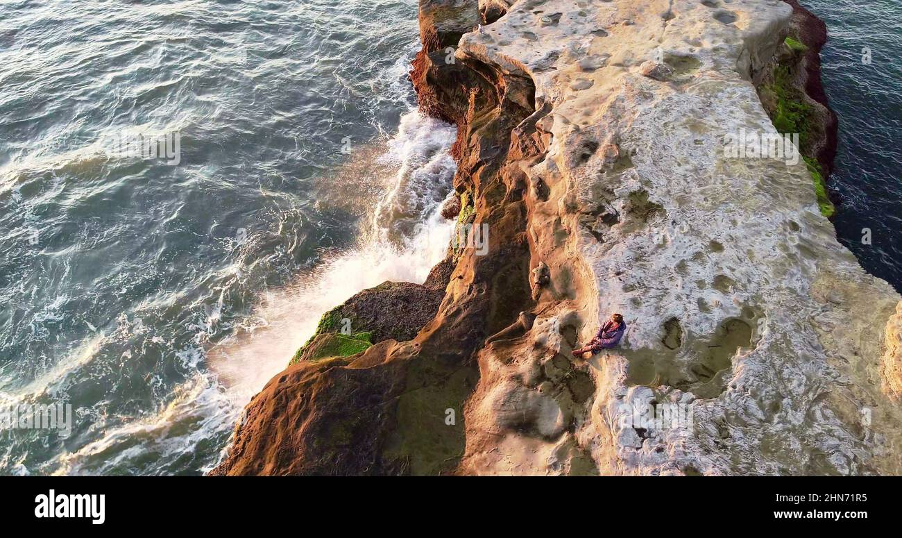 Aerial view of woman sitting on cliff edge, watching sunset at Sunset ...