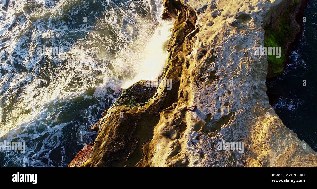 Aerial view of woman sitting on cliff edge, watching sunset at Sunset ...