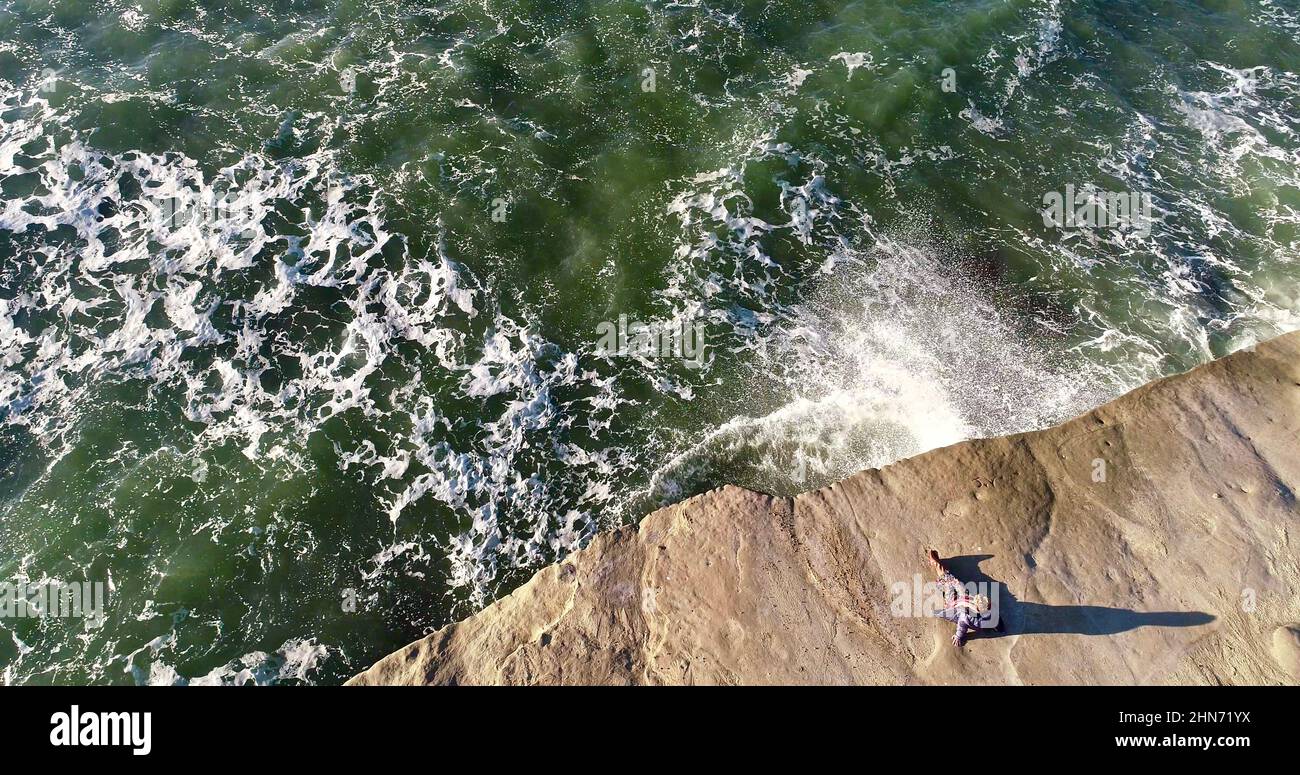 Aerial view of woman sitting on cliff edge, watching sunset at Sunset ...