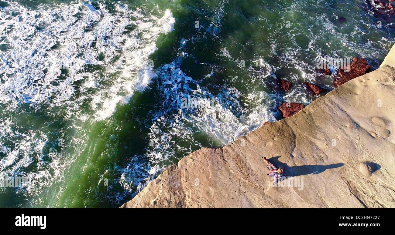 Aerial view of woman sitting on cliff edge, watching sunset at Sunset ...