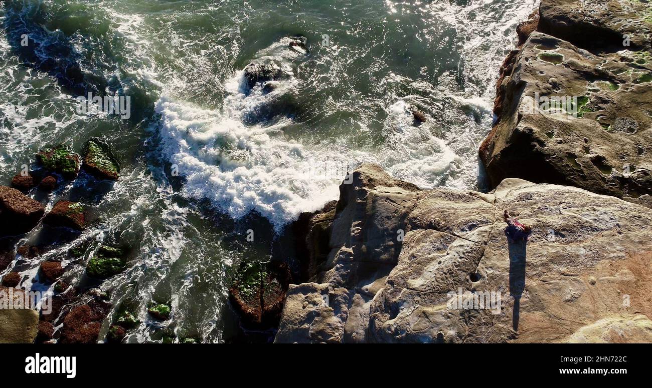 Aerial view of woman sitting on cliff edge, watching sunset at Sunset ...