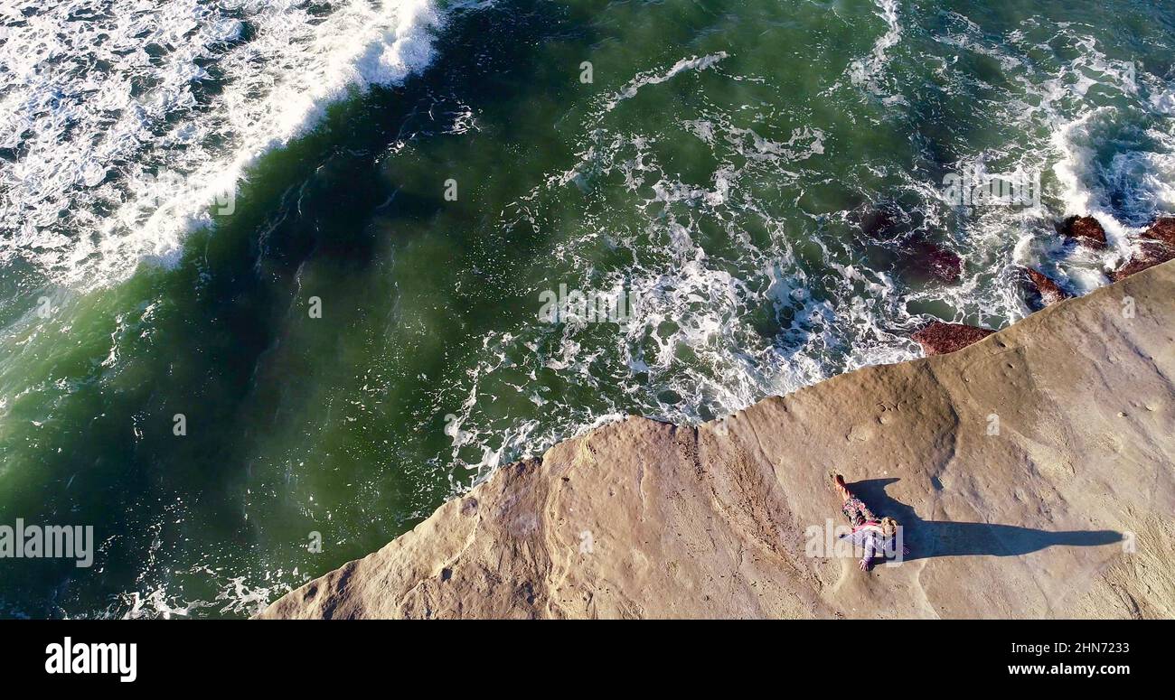 Aerial view of woman sitting on cliff edge, watching sunset at Sunset ...