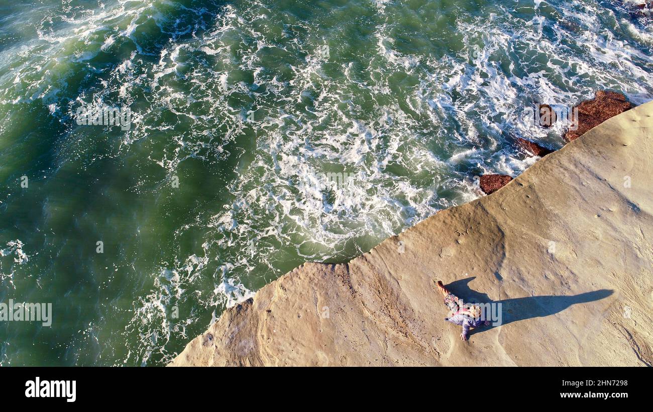 Aerial view of woman sitting on cliff edge, watching sunset at Sunset ...