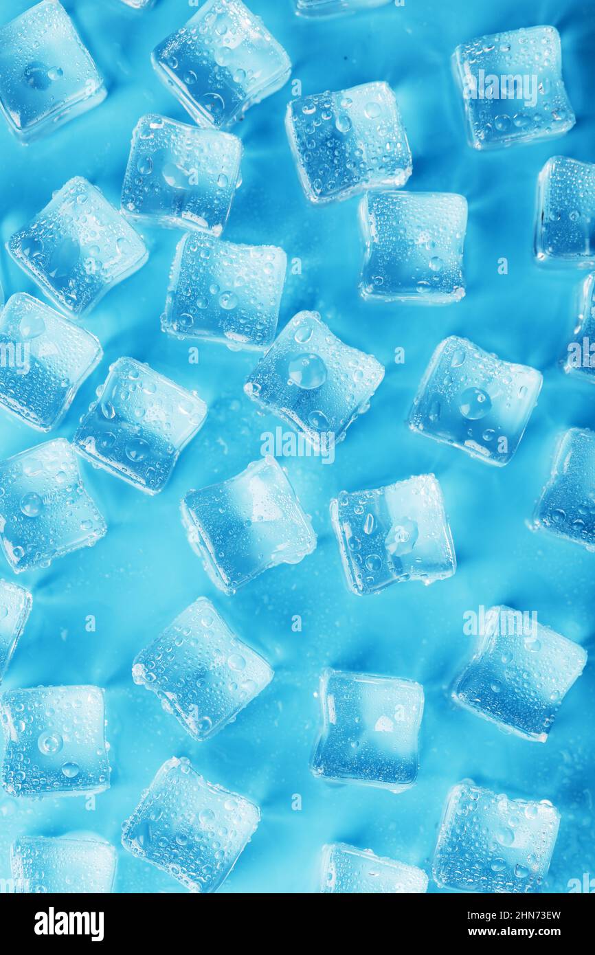 Many frosty and refreshing ice cubes with drops on a blue background ...