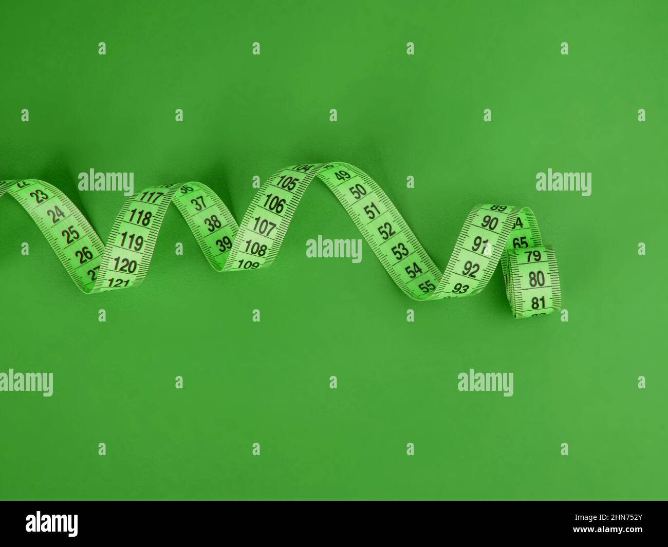 Green tape measure on the green background Stock Photo - Alamy