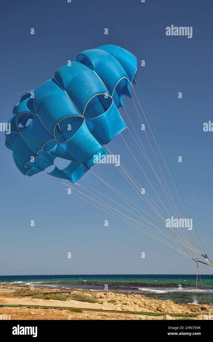 Blue open parachute for paragliding watersports against clear blue sky ...