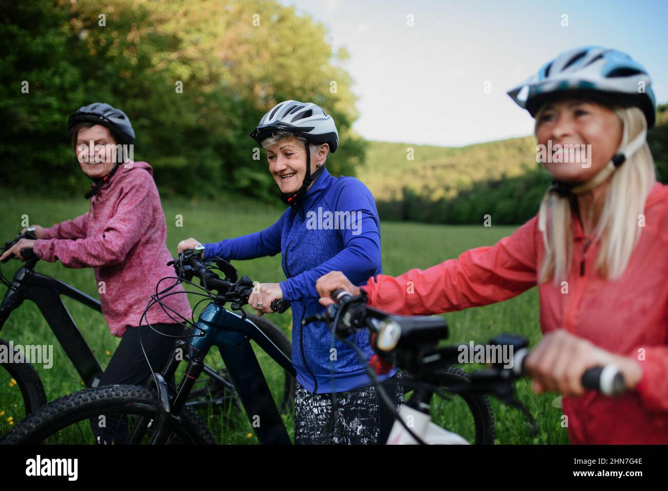 Happy active senior women friends pushing bicycles together outdoors in ...