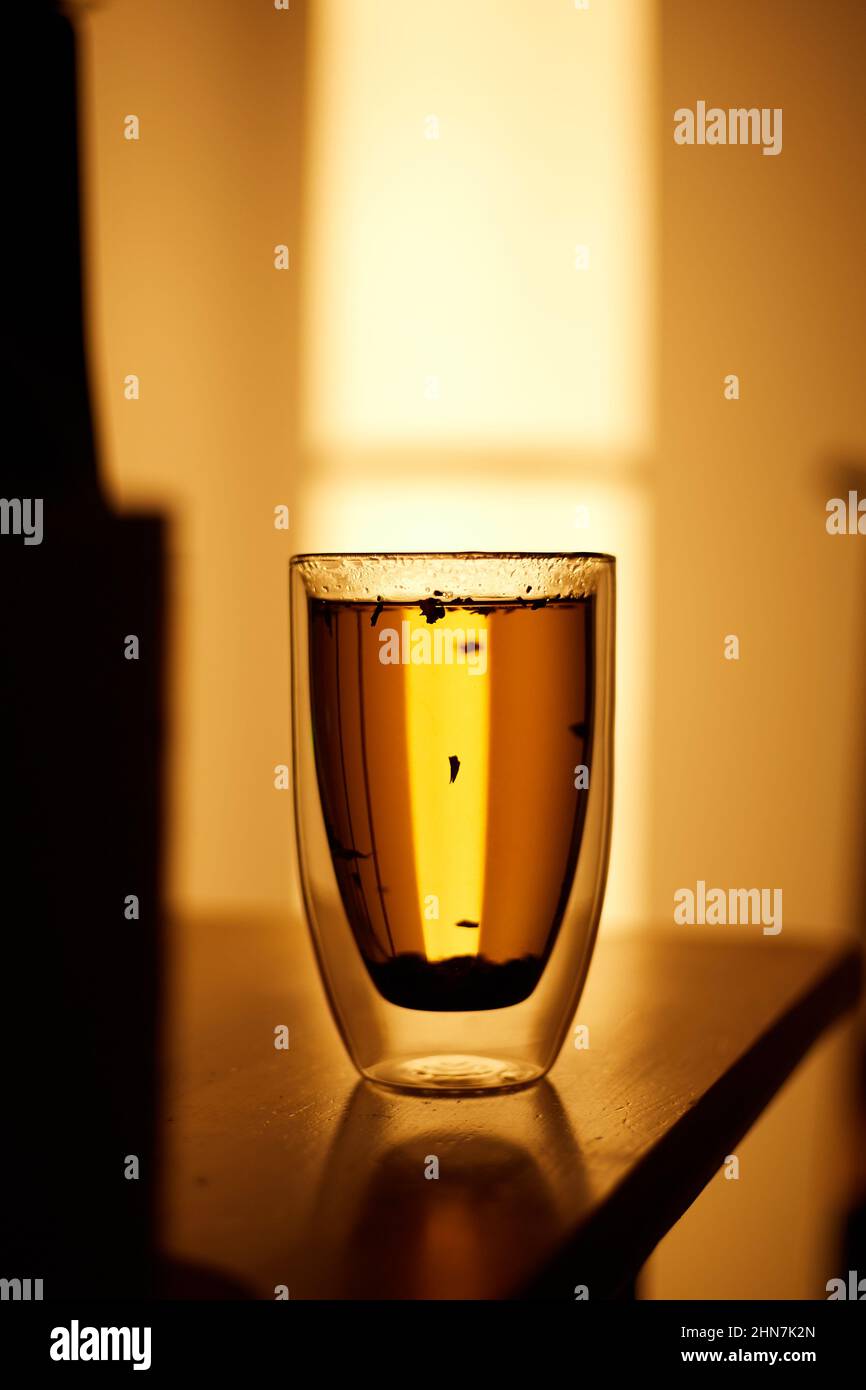 A glass of tea with floating tea leaves on a table with a light behind ...