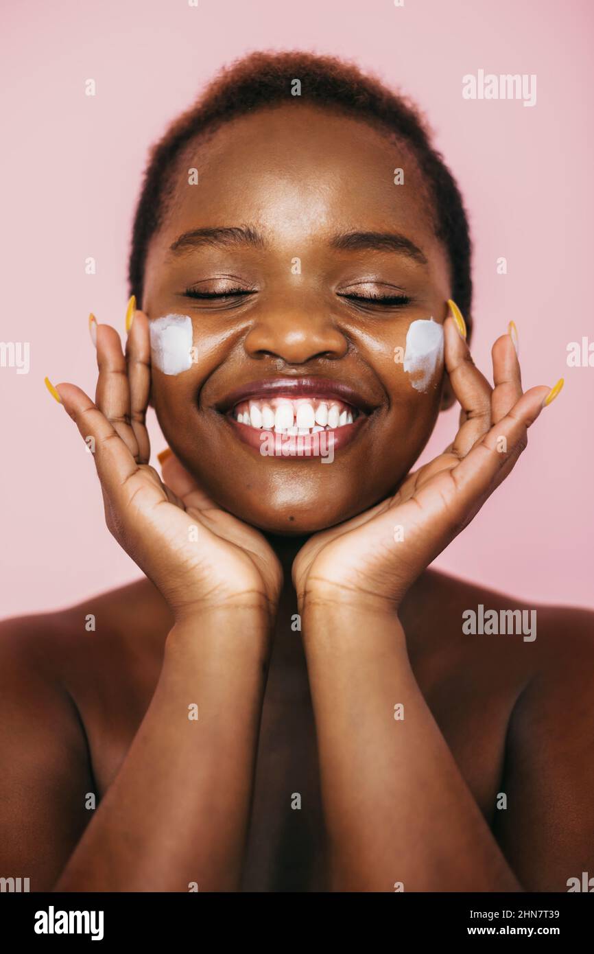 Laughing woman with applying moisturizing cream on her face isolated ...