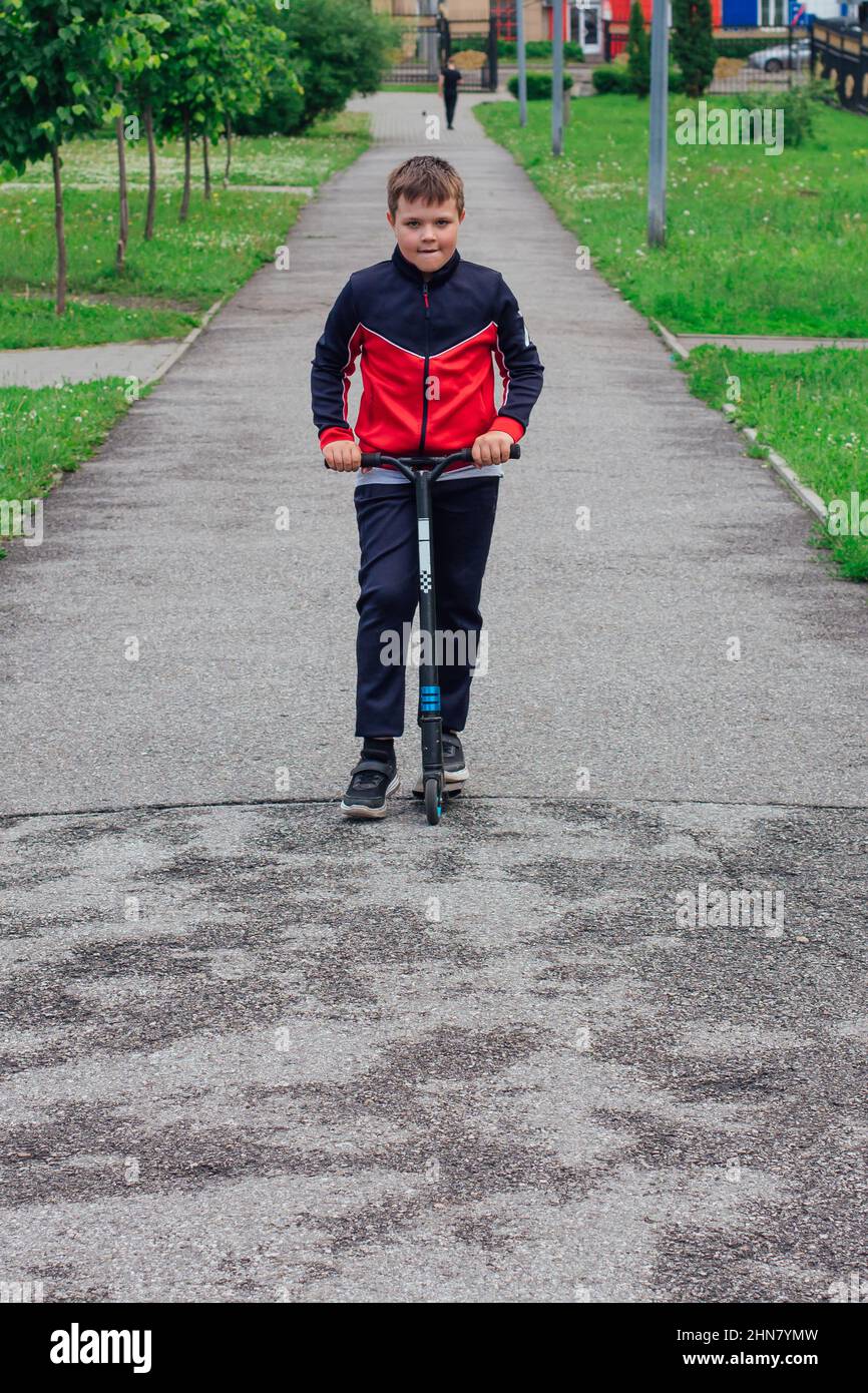 Cute boy riding scooter in a summer park. Happy teenager riding a ...