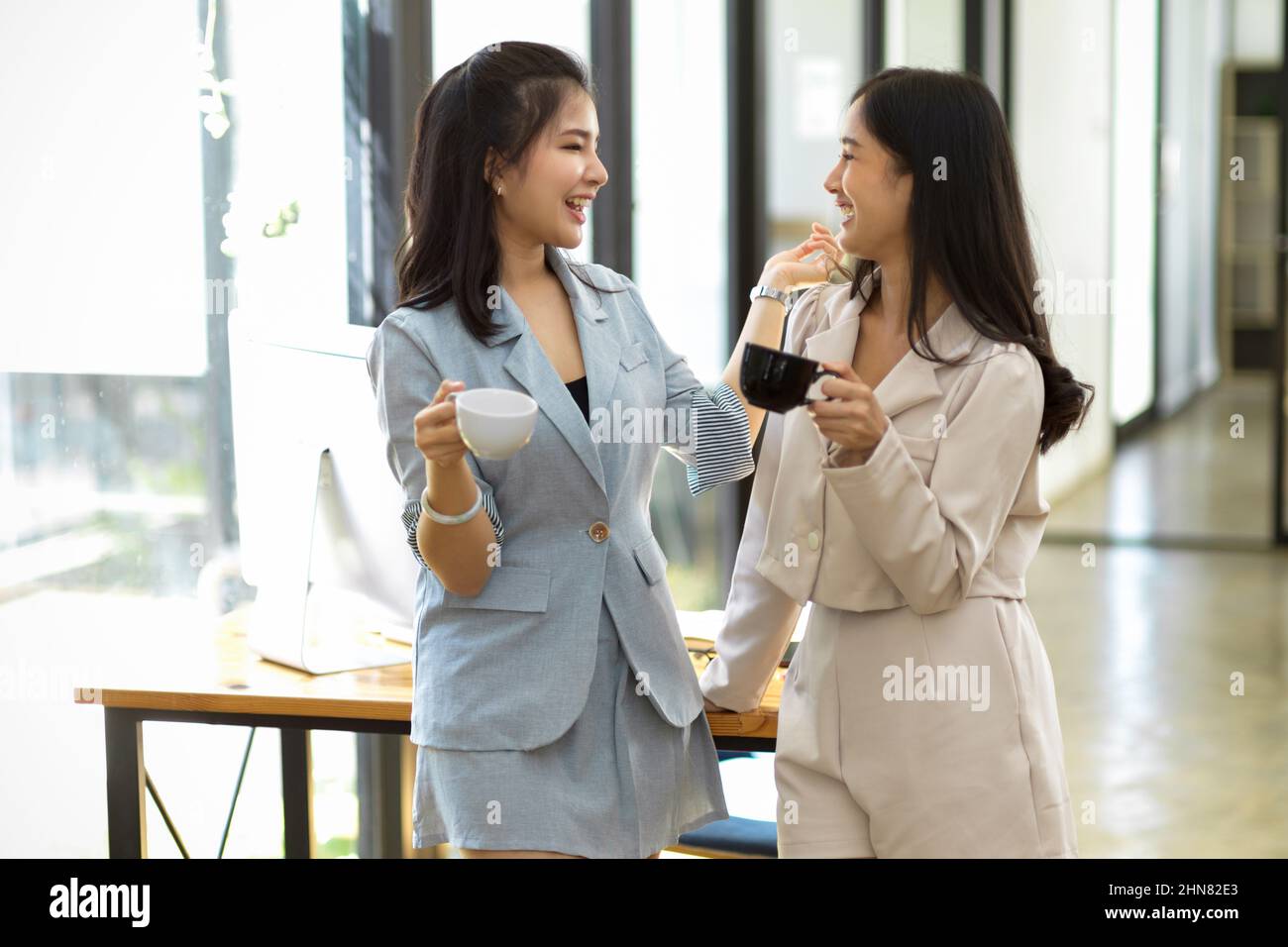 Two beautiful Asian young business employees chatting during a coffee ...