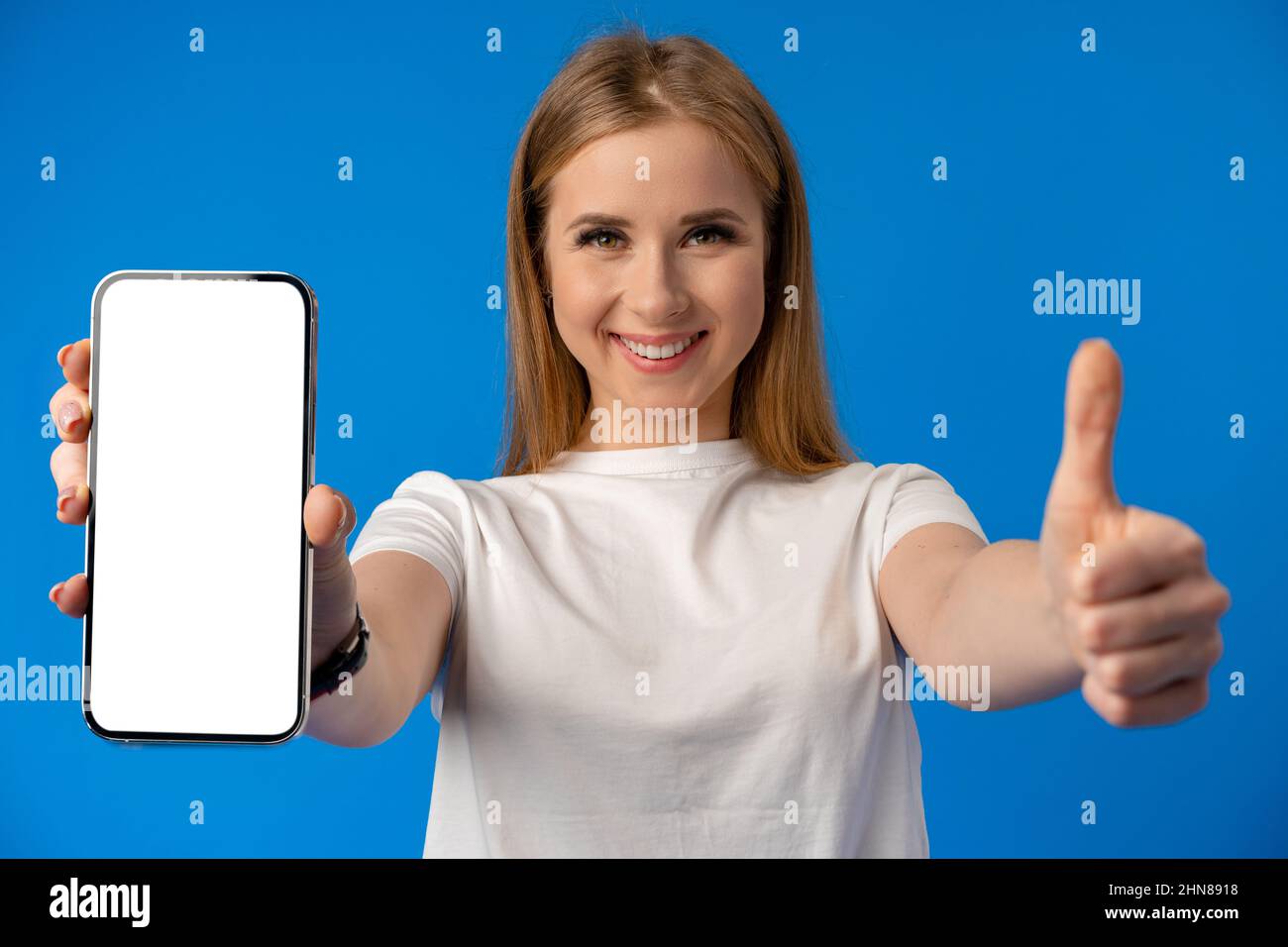 Young woman point finger at isolated smartphone screen over blue color ...