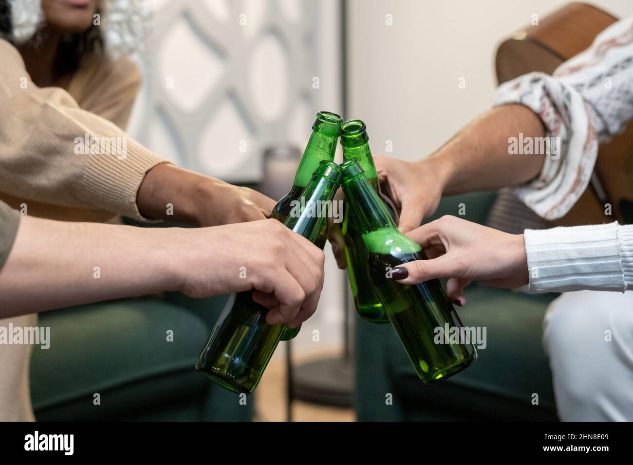 Close-up of young people toasting with bottles of beer during a party ...