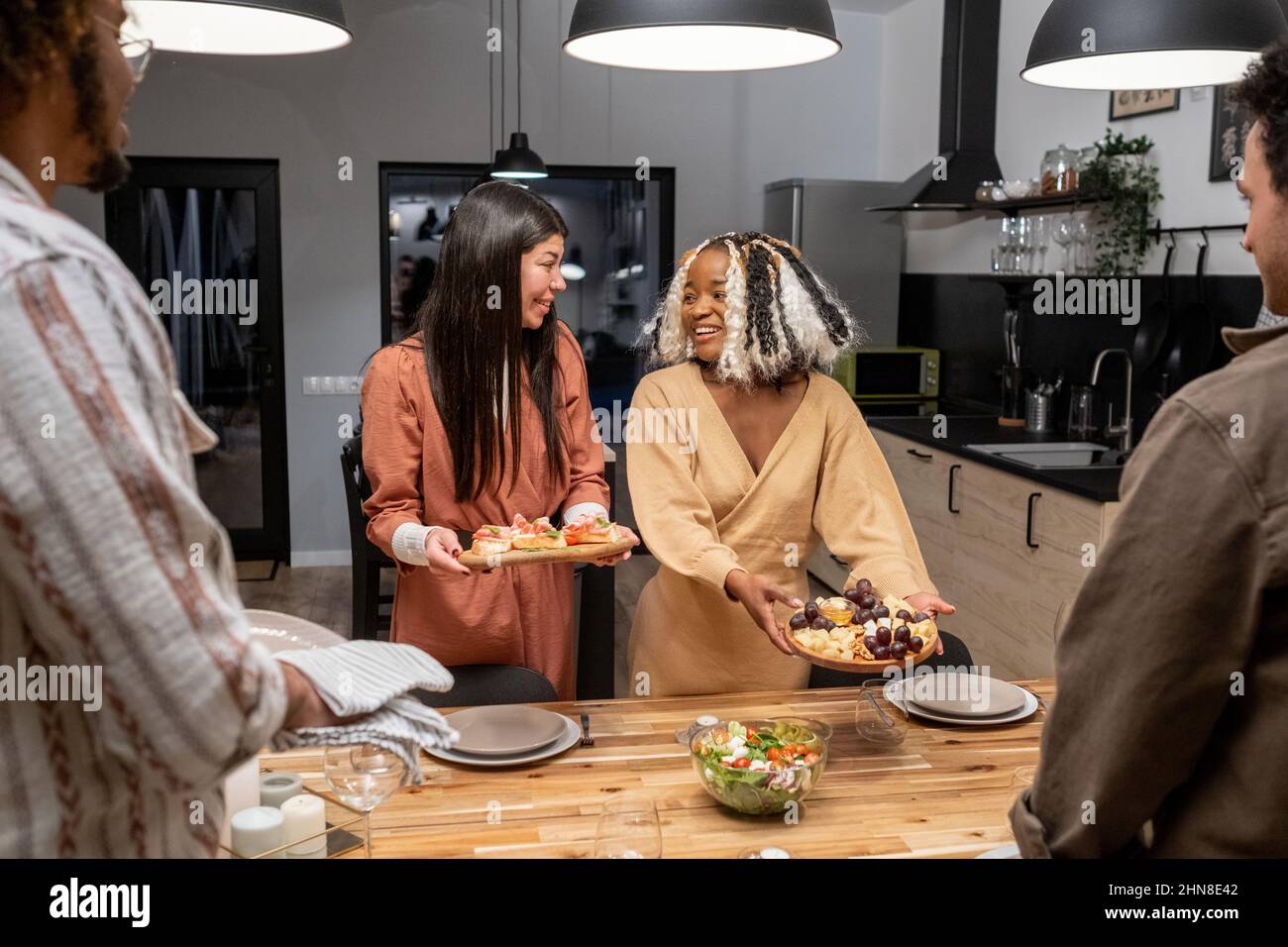Happy young women holding plates with appetizers and putting them on ...
