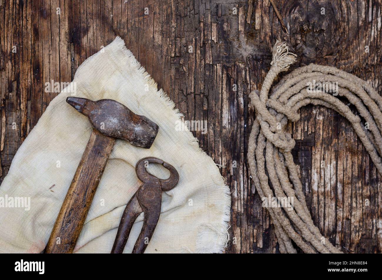 An old hand tool, a roll of rope, and a tattered rag on a dark wooden ...