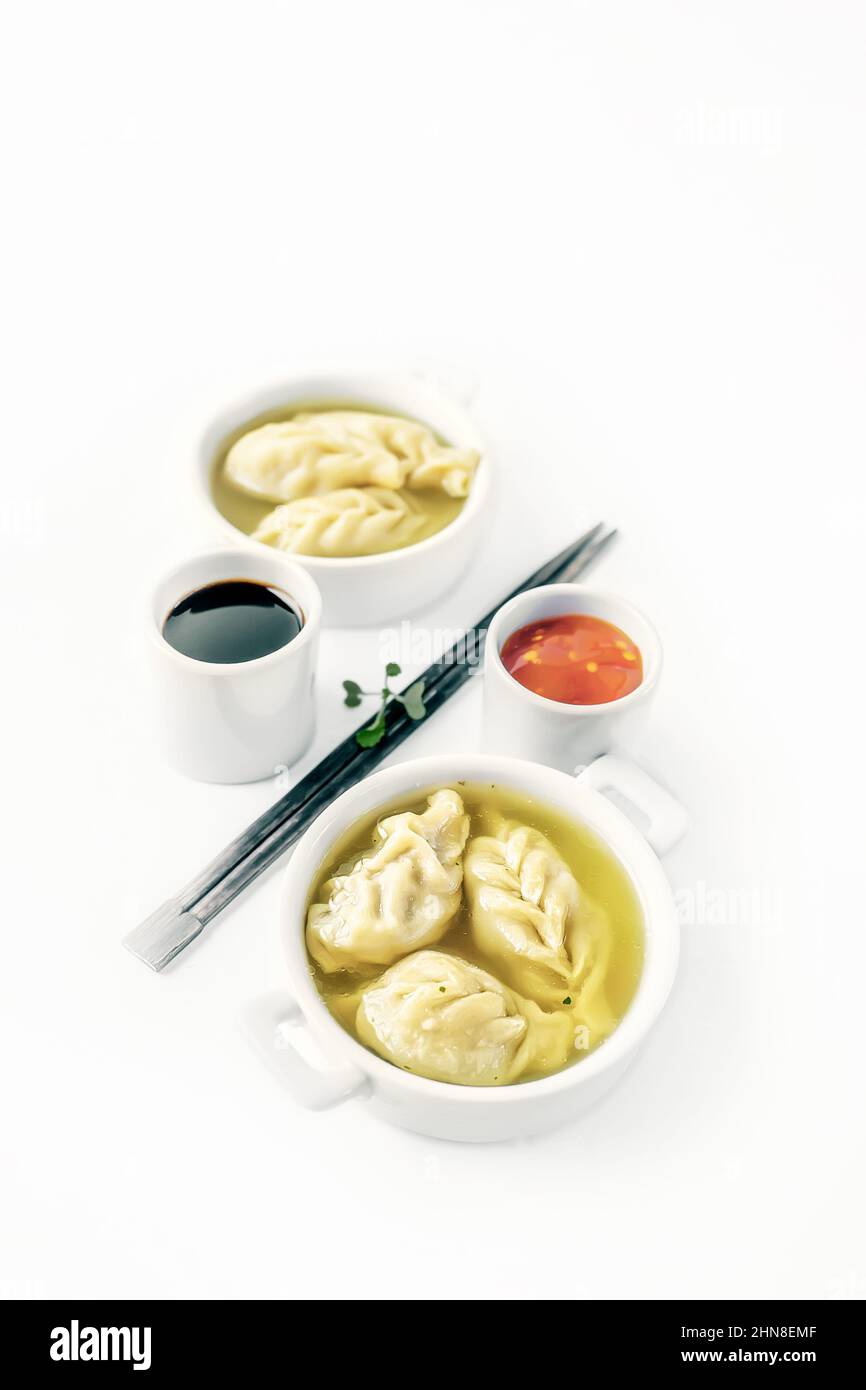 Dumplings are served in white cups with sauces on a serving board . Top ...