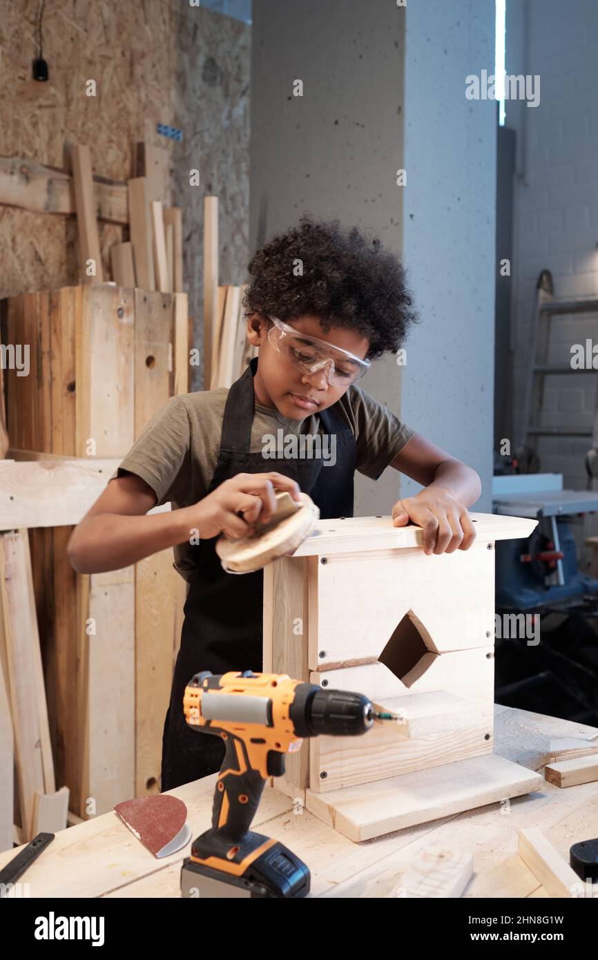 Vertical portrait of young black boy building wooden birdhouse in ...