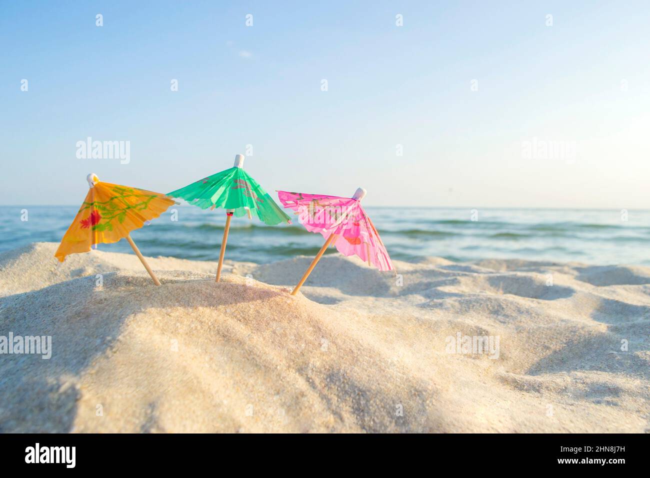 Three paper cocktail multi-colored umbrellas on sandy sea beach with ...