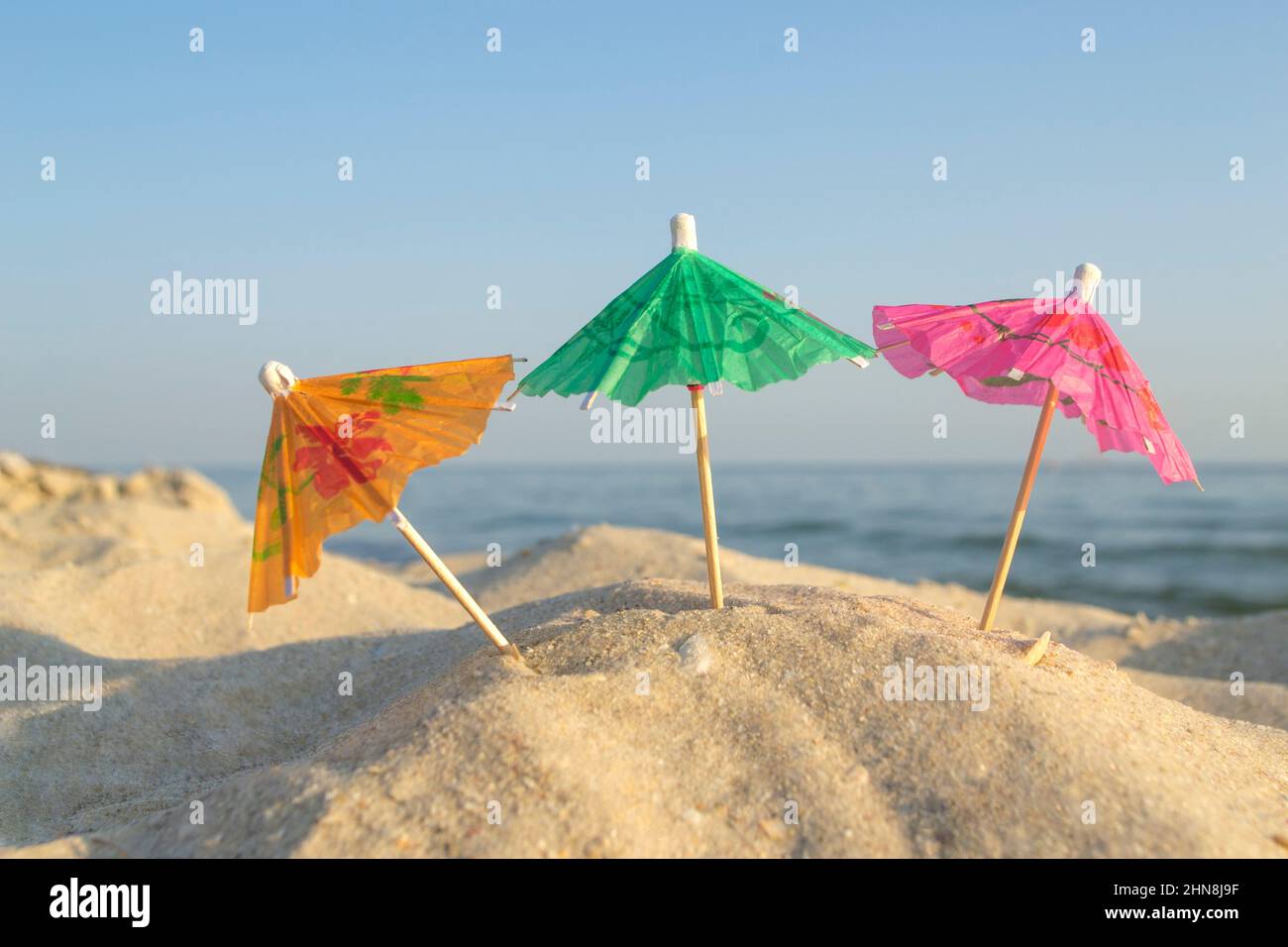 Three paper cocktail multi-colored umbrellas on sandy sea beach with ...