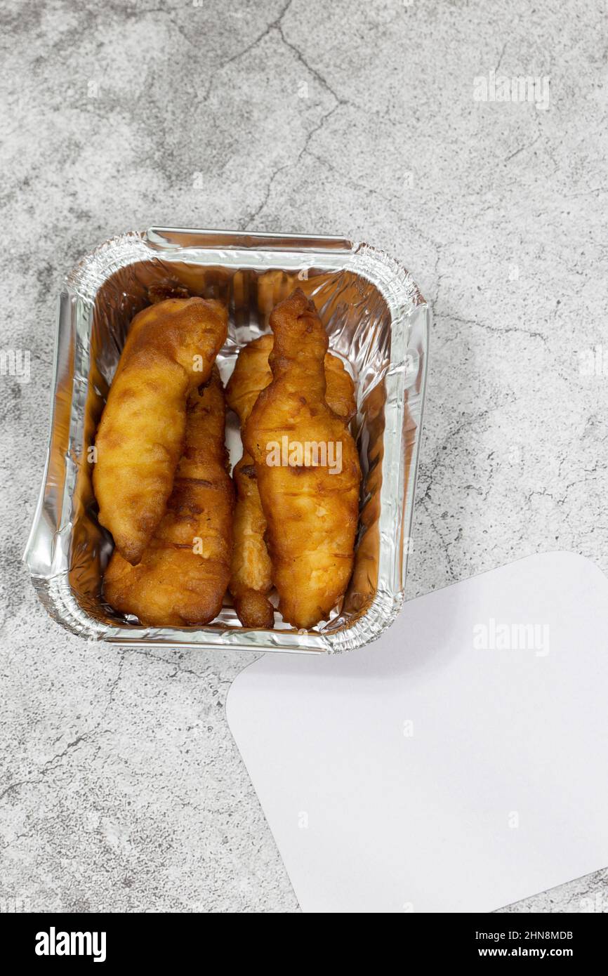 Battered chicken portions in a foil takeaway tray with lid. On a ...