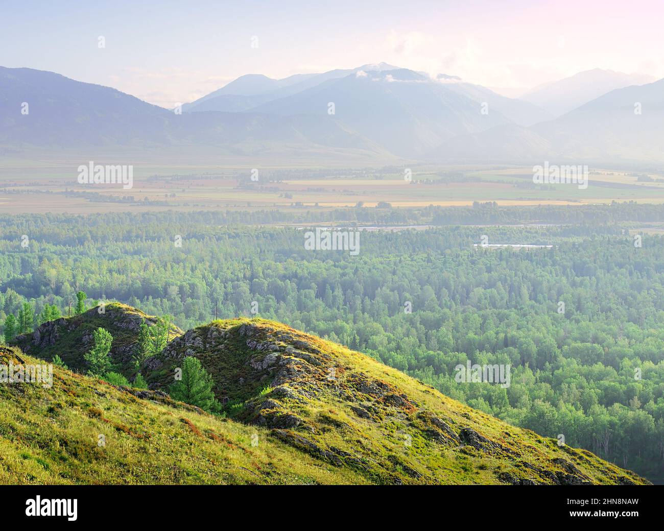 A green mountain slope above a mountain plain under a blue sky ...