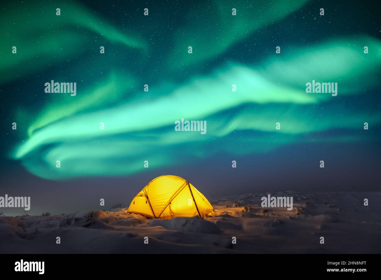 Yellow tent lighted from the inside against the backdrop of incredible starry sky with Aurora ...