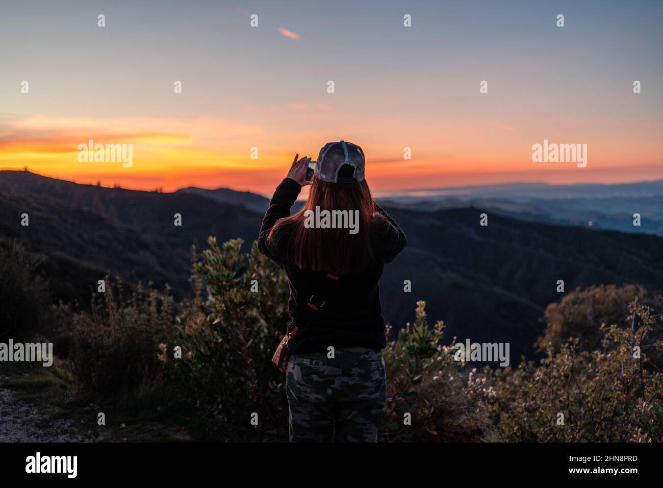 Woman takes a picture of the sunset over a mountainside view Stock ...