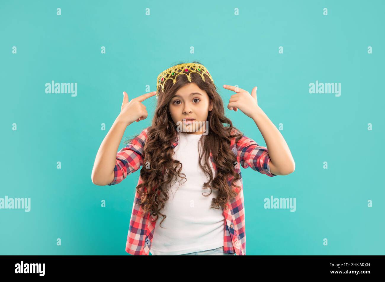 confused teen girl with curly hair point finger on crown on blue ...