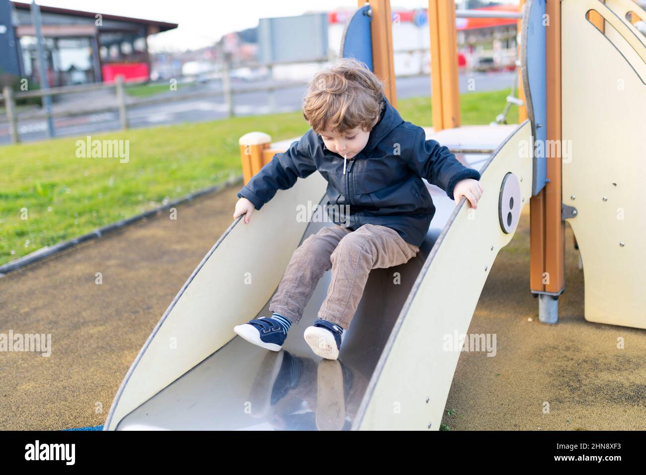 three year old boy in the park playing going down the slide after ...