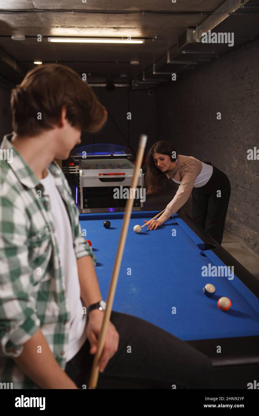 Vertical Shot Of A Young Man Watching His Girlfriend Striking Billiad Ball With A Cue While