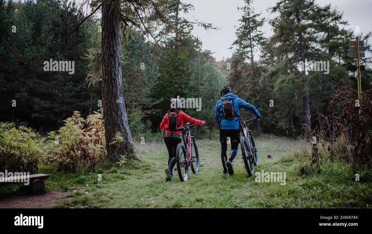 Rear view of senior couple bikers walking and pushing e-bikes outdoors ...
