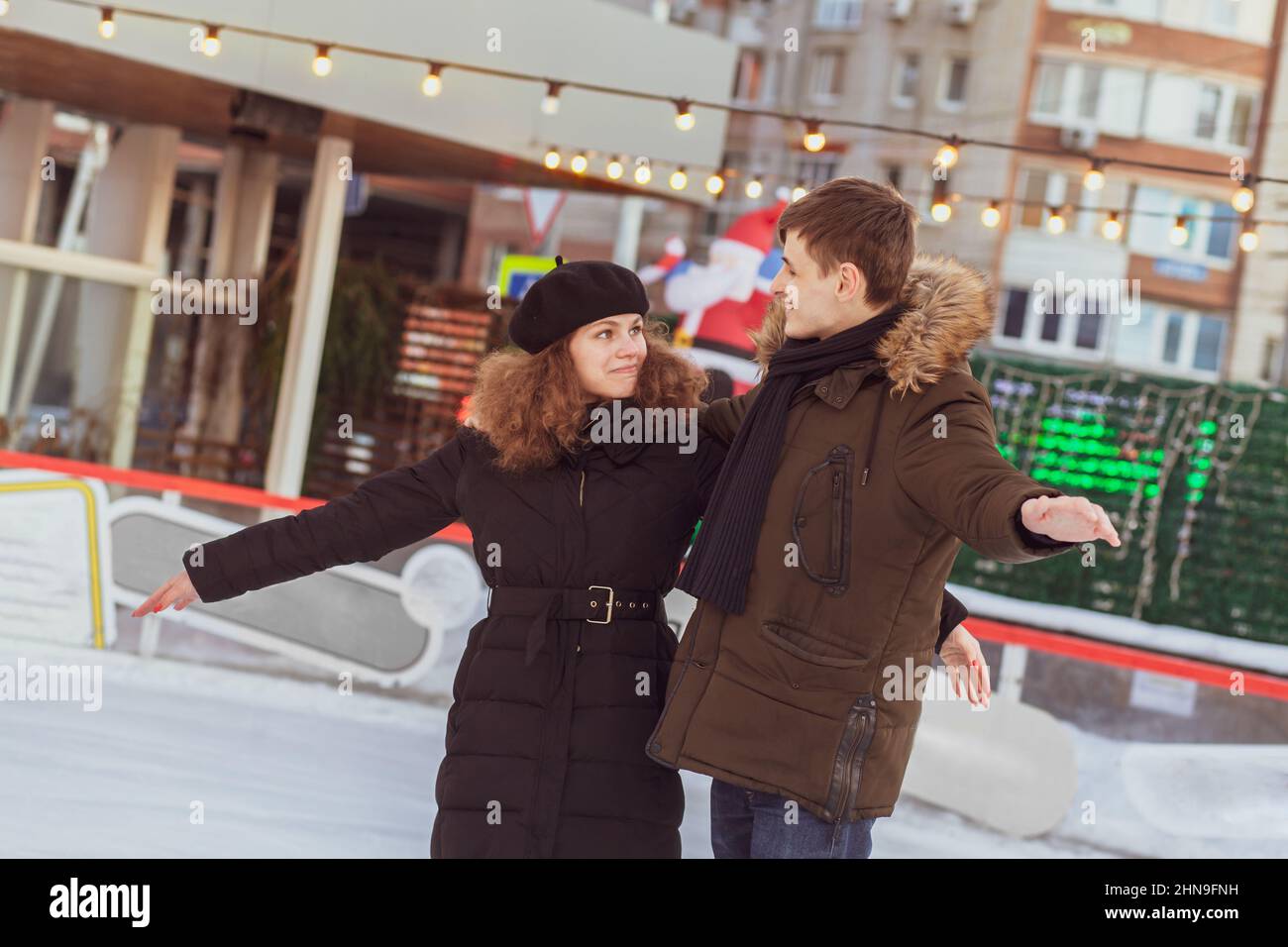 A young couple in love skating on a skating rink, arms apart, look at ...
