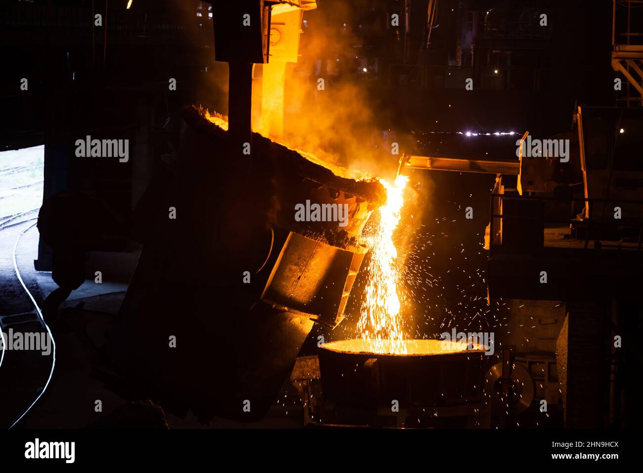 Molten metal pouring from metallurgy ladle. Smoke, on black background ...