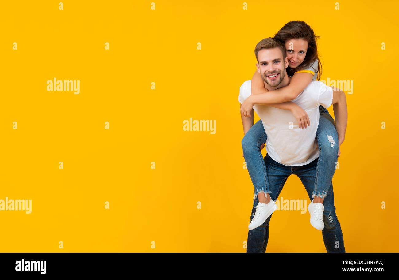 Happy romantic couple having fun doing piggyback ride yellow background ...