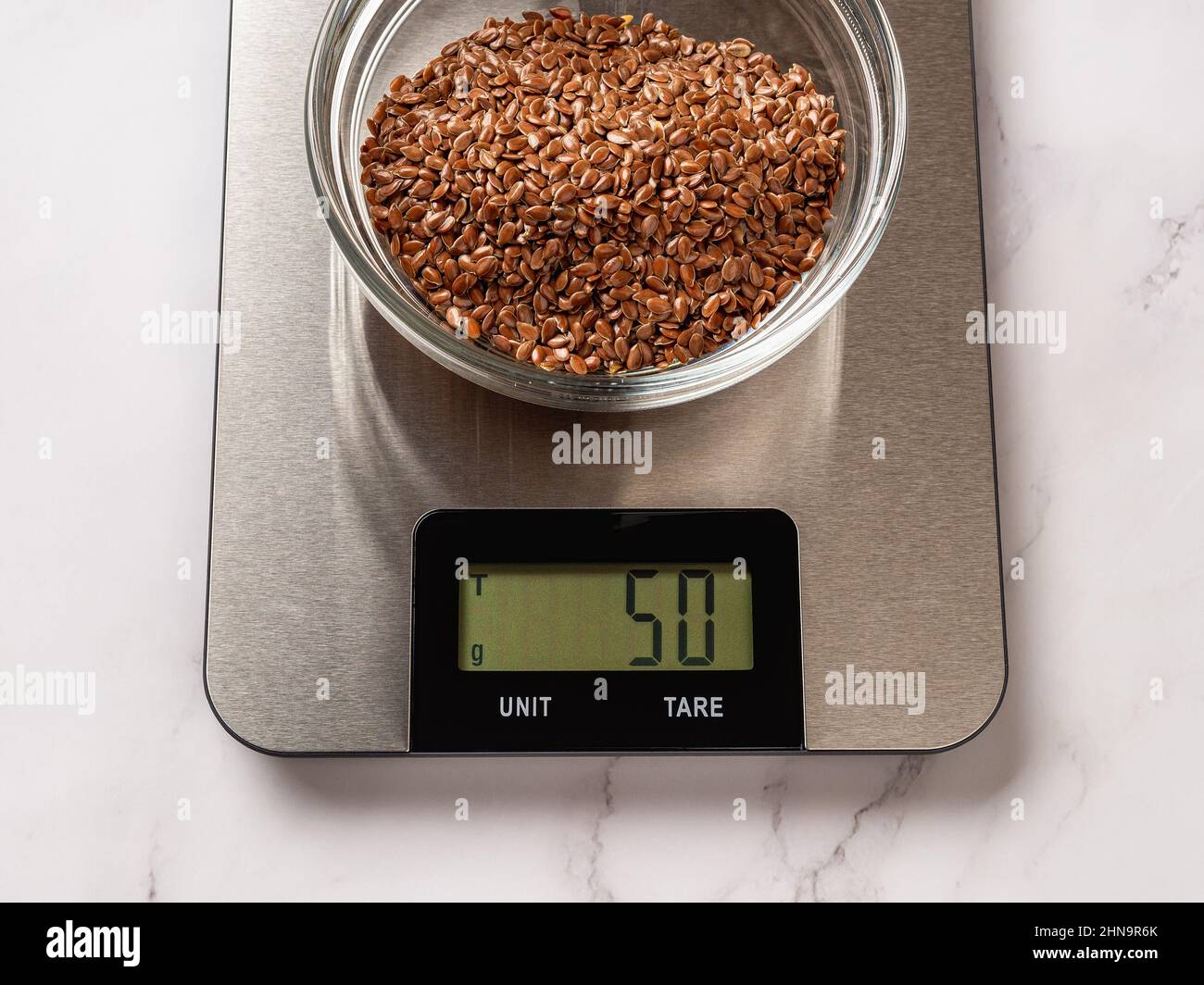 Raw flax seeds in a glass bowl on a digital kitchen scale. 50g flax ...